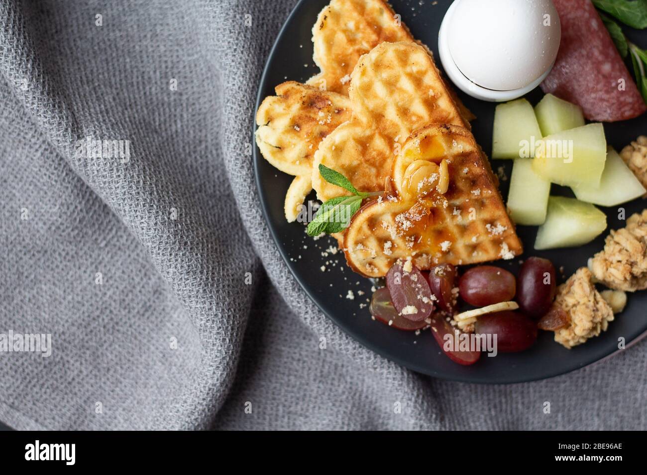 Stunning hearty breakfast on dark plate on bed with gray bedspread in ...