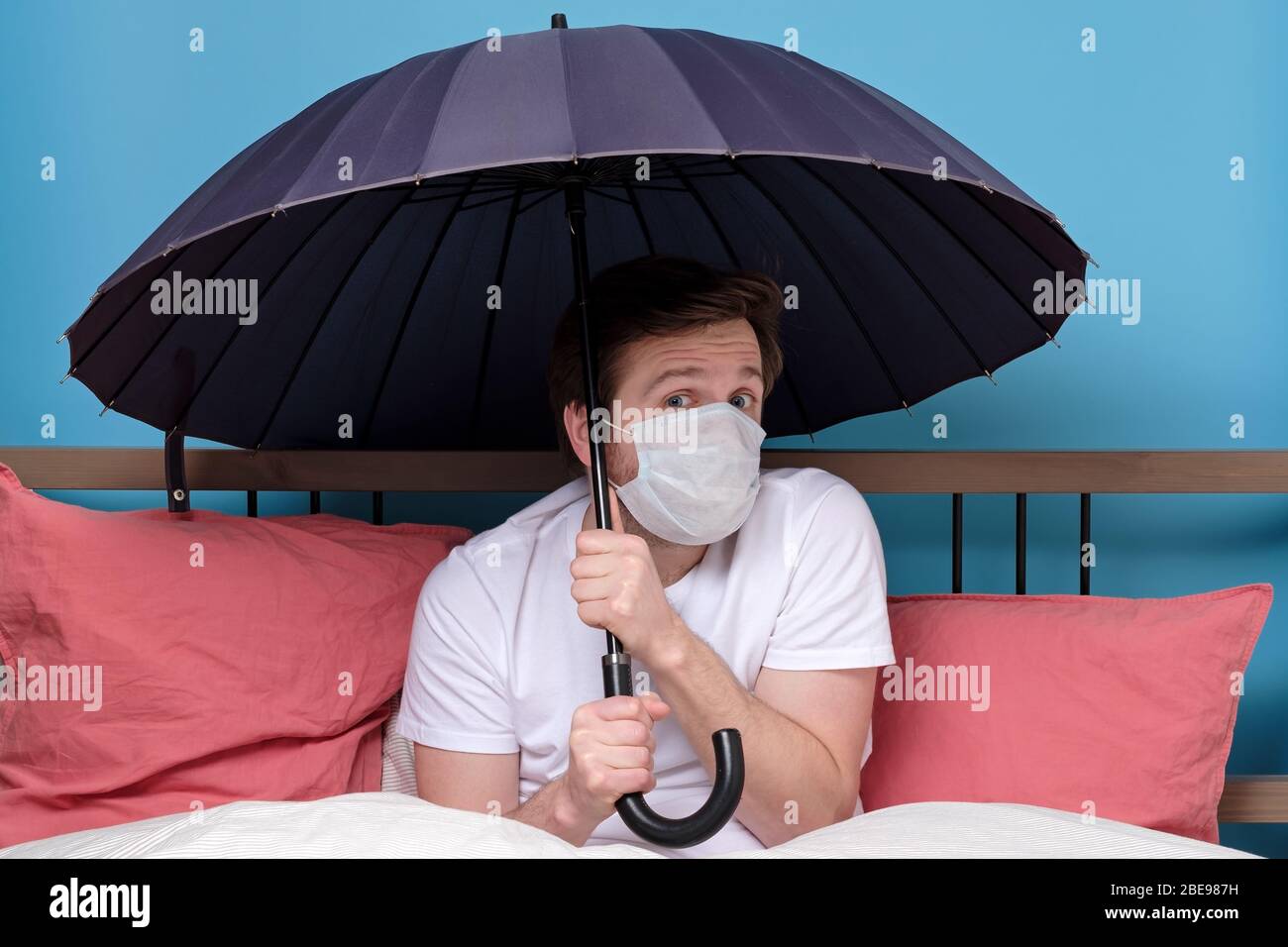 Man in medical mask holding an umbrella sitting at the bed alone Stock ...