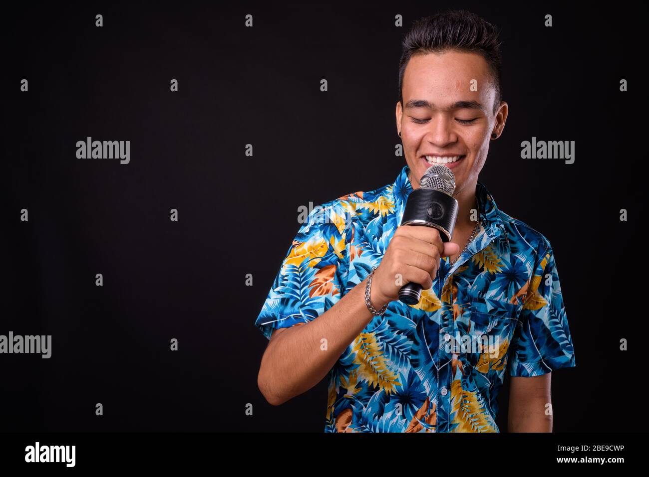 Portrait of happy young Indian tourist man singing with microphone ...