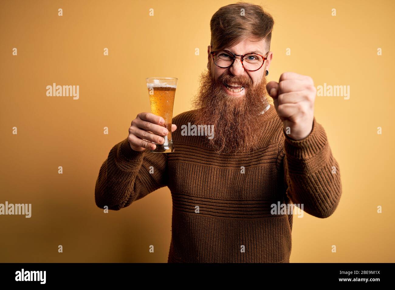 Irish redhead man with beard drinking a glass of refreshing beer over ...