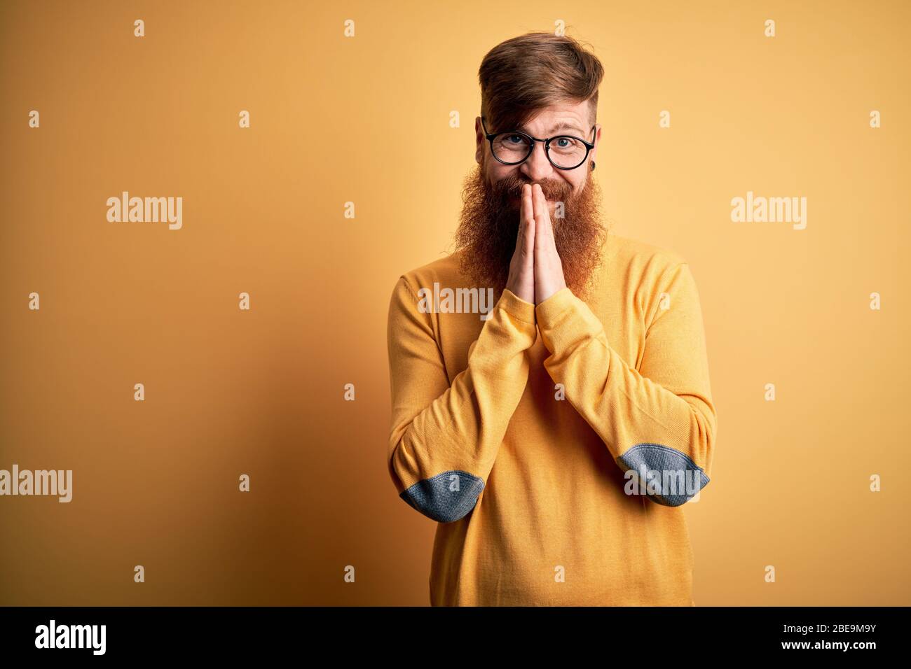 Handsome Irish redhead man with beard wearing glasses over yellow ...