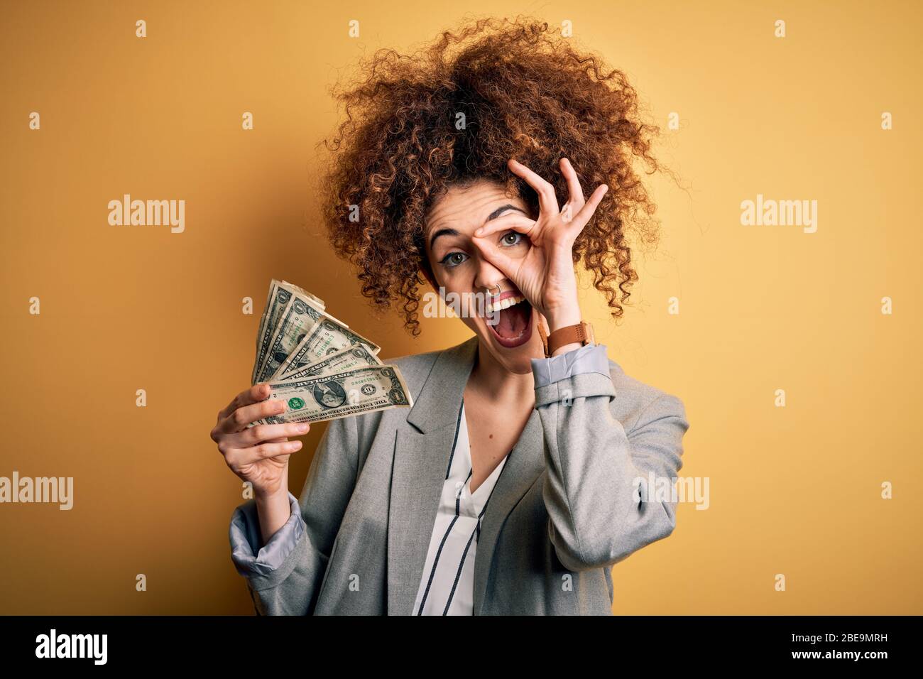 Young beautiful woman with curly hair and piercing holding dollars ...