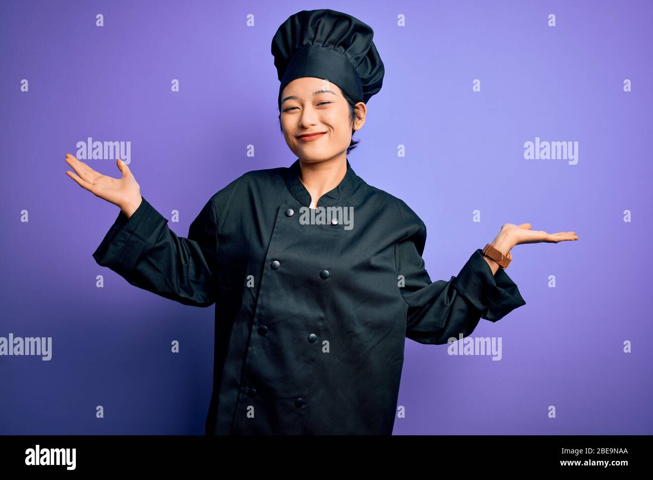 Young beautiful chinese chef woman wearing cooker uniform and hat over ...