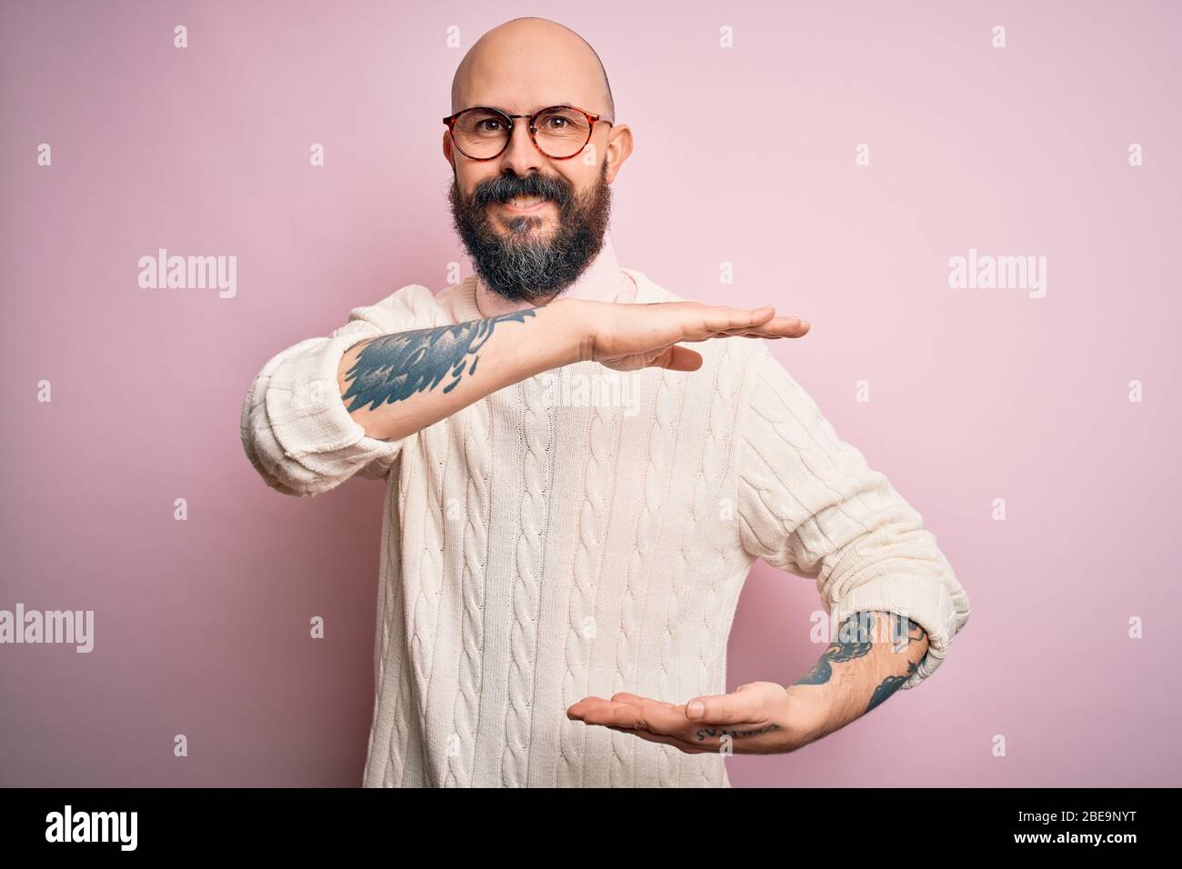 Handsome bald man with beard and tattoo wearing glasses and sweater ...