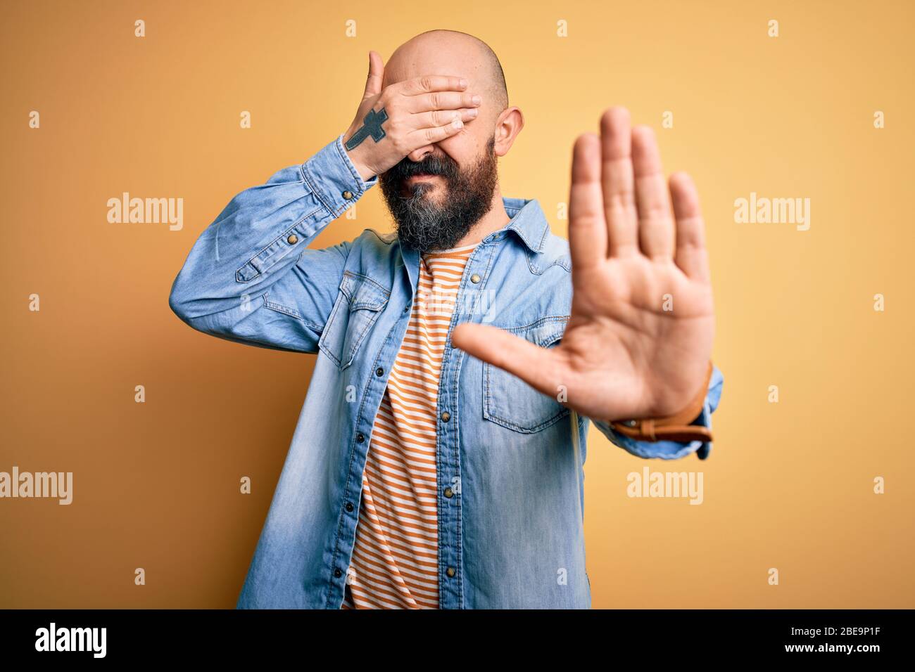 Handsome bald man with beard wearing casual denim jacket and striped t ...