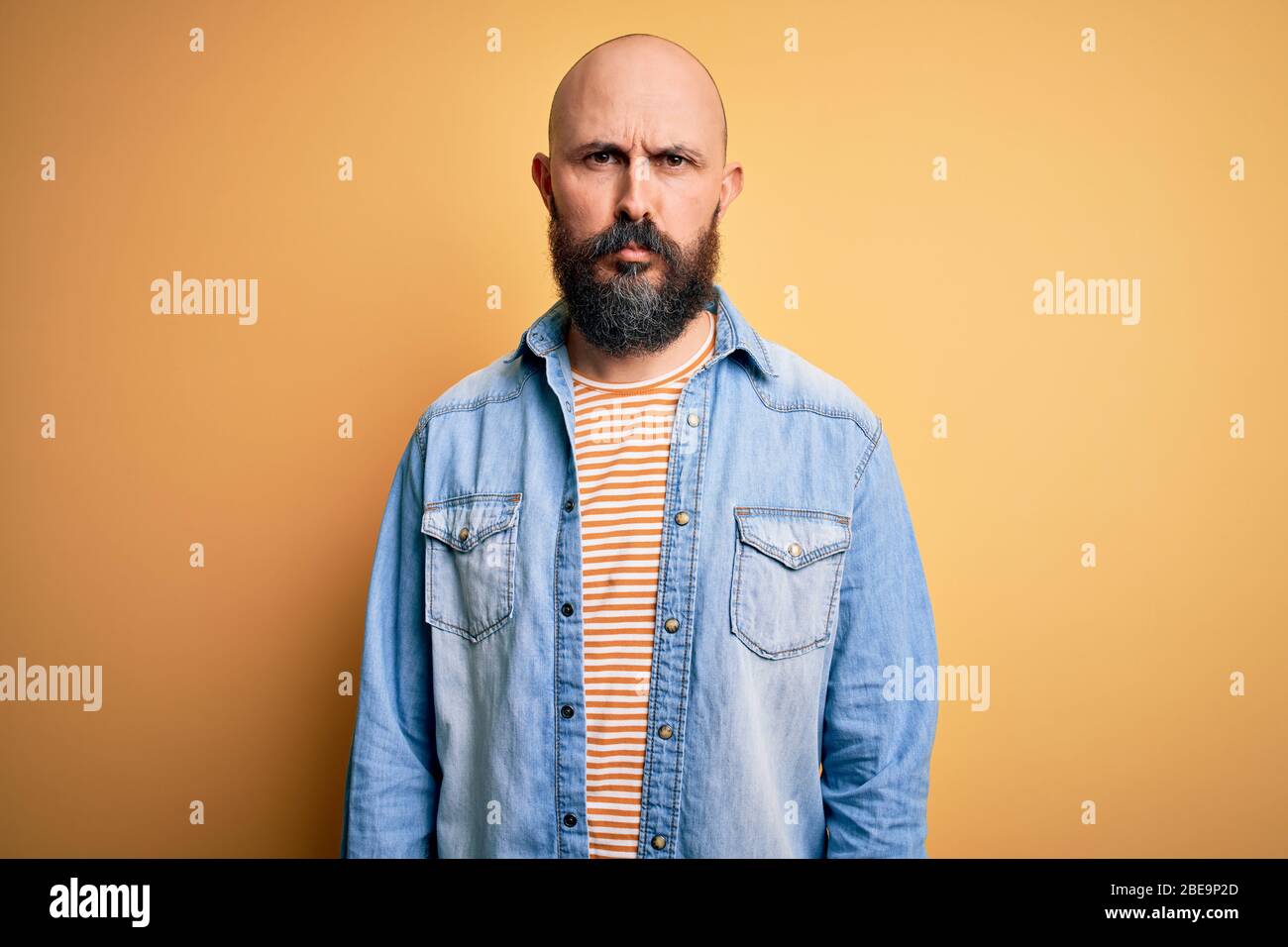 Handsome bald man with beard wearing casual denim jacket and striped t ...