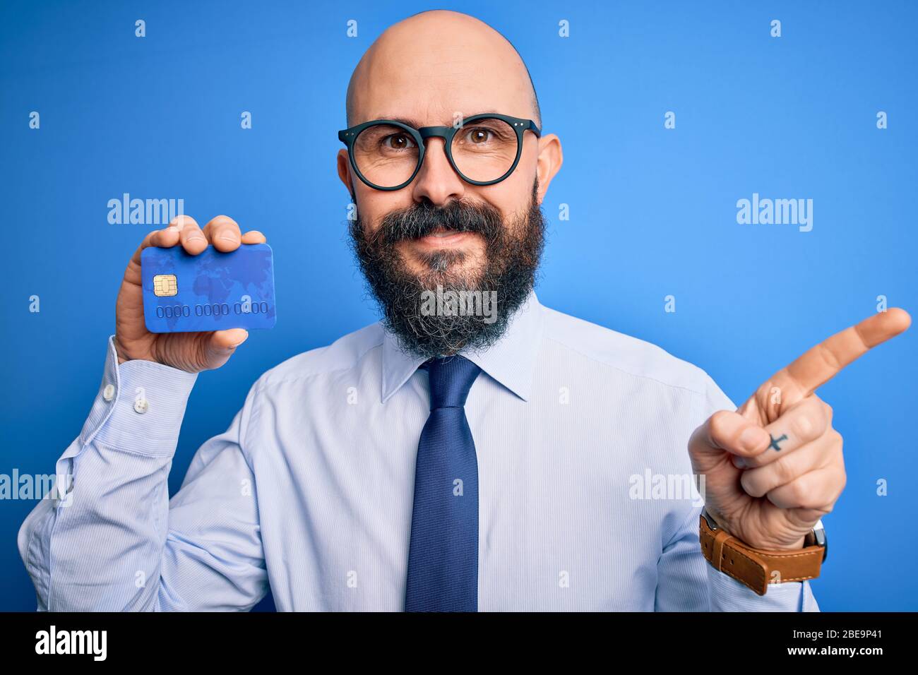 Handsome bald business man with beard holding credit card over isolated ...