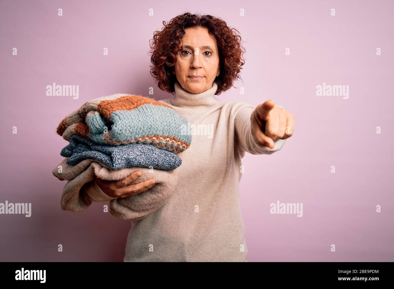 Middle age curly hair housework woman holding pile of clothes over ...