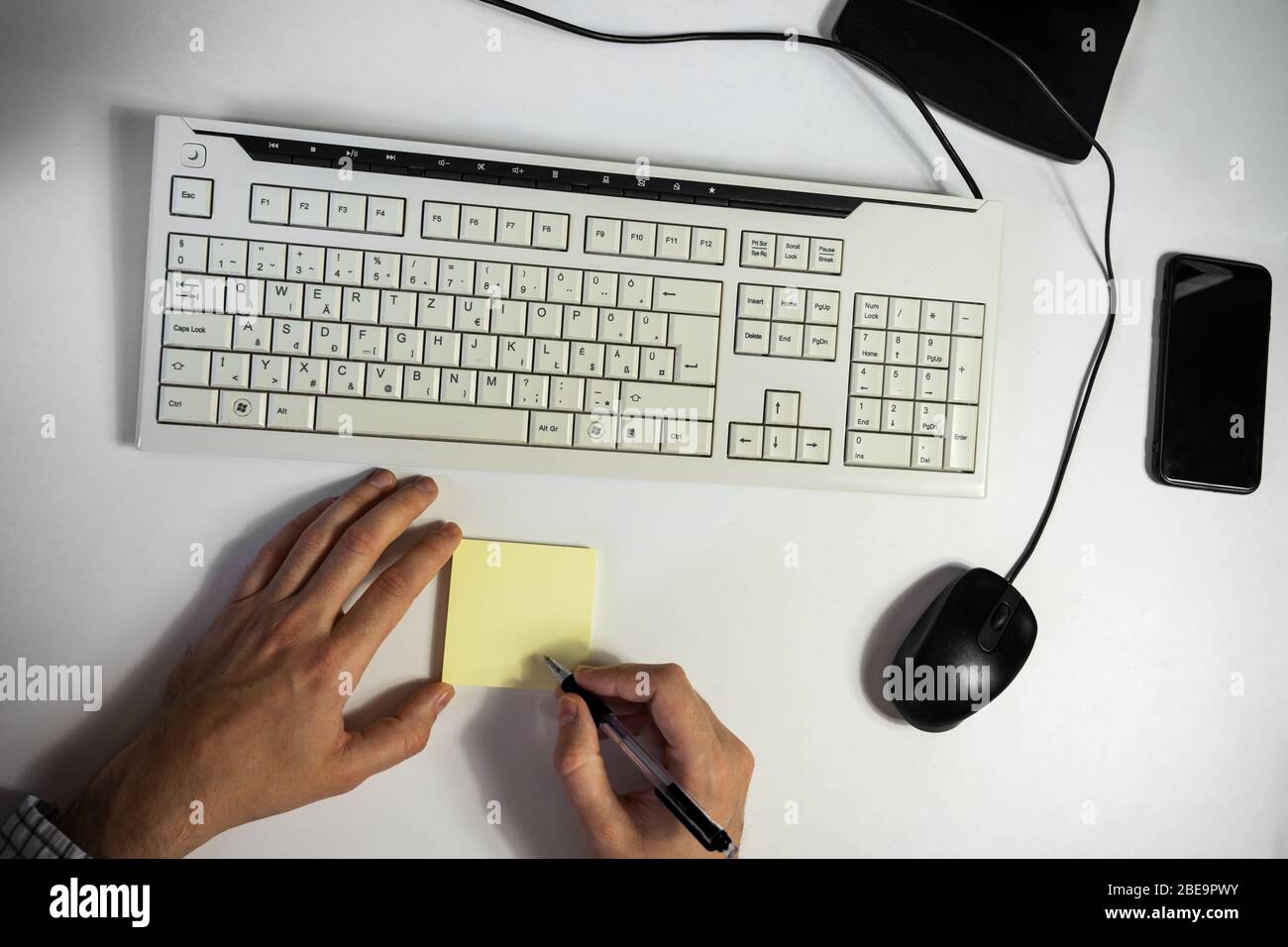 Man in home office writing a reminder post it note on his desk in ...