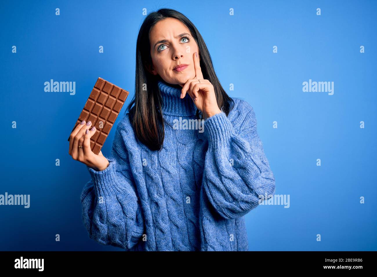 Young woman with blue eyes holding sweet chocolate bar standing over ...
