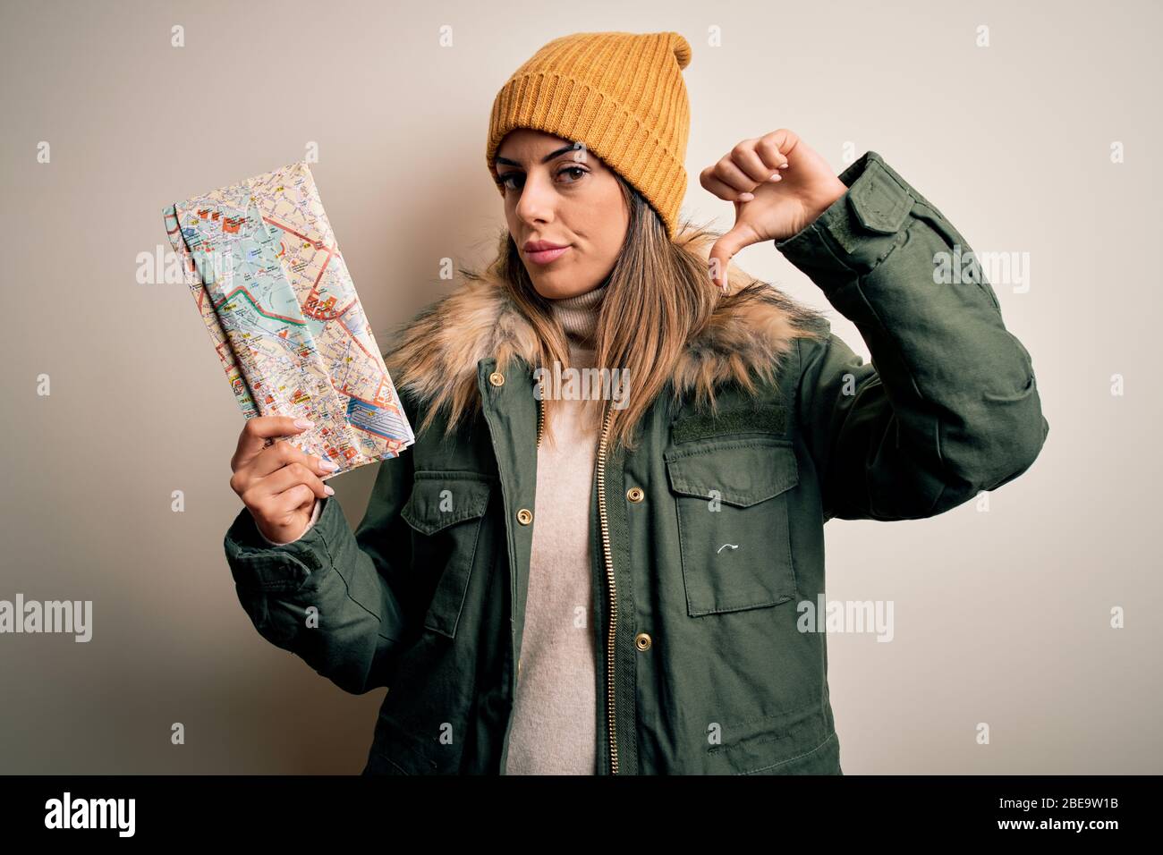 Young beautiful tourist woman wearing winter clothes holding city map ...