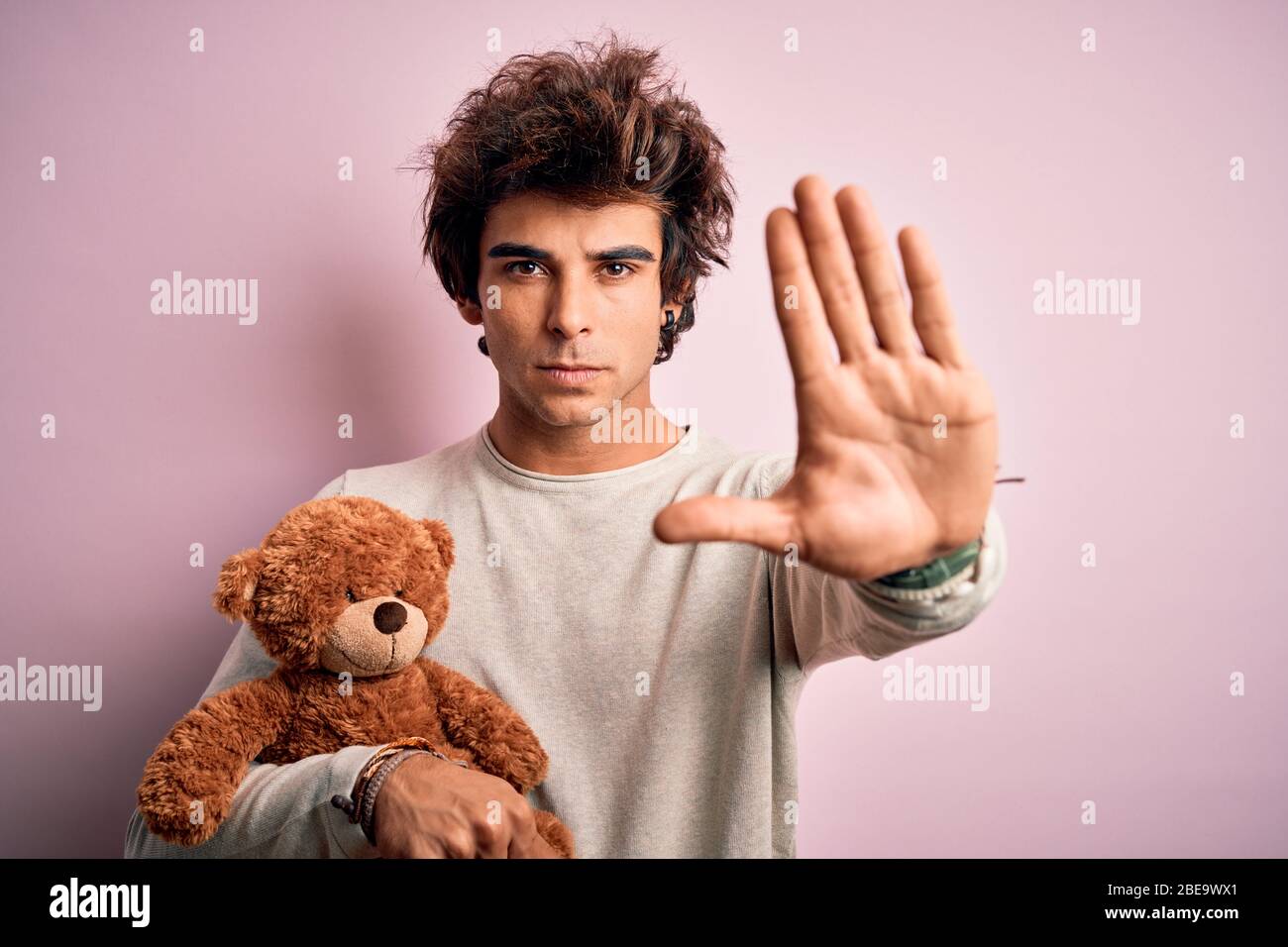 Young handsome man holding teddy bear standing over isolated pink ...