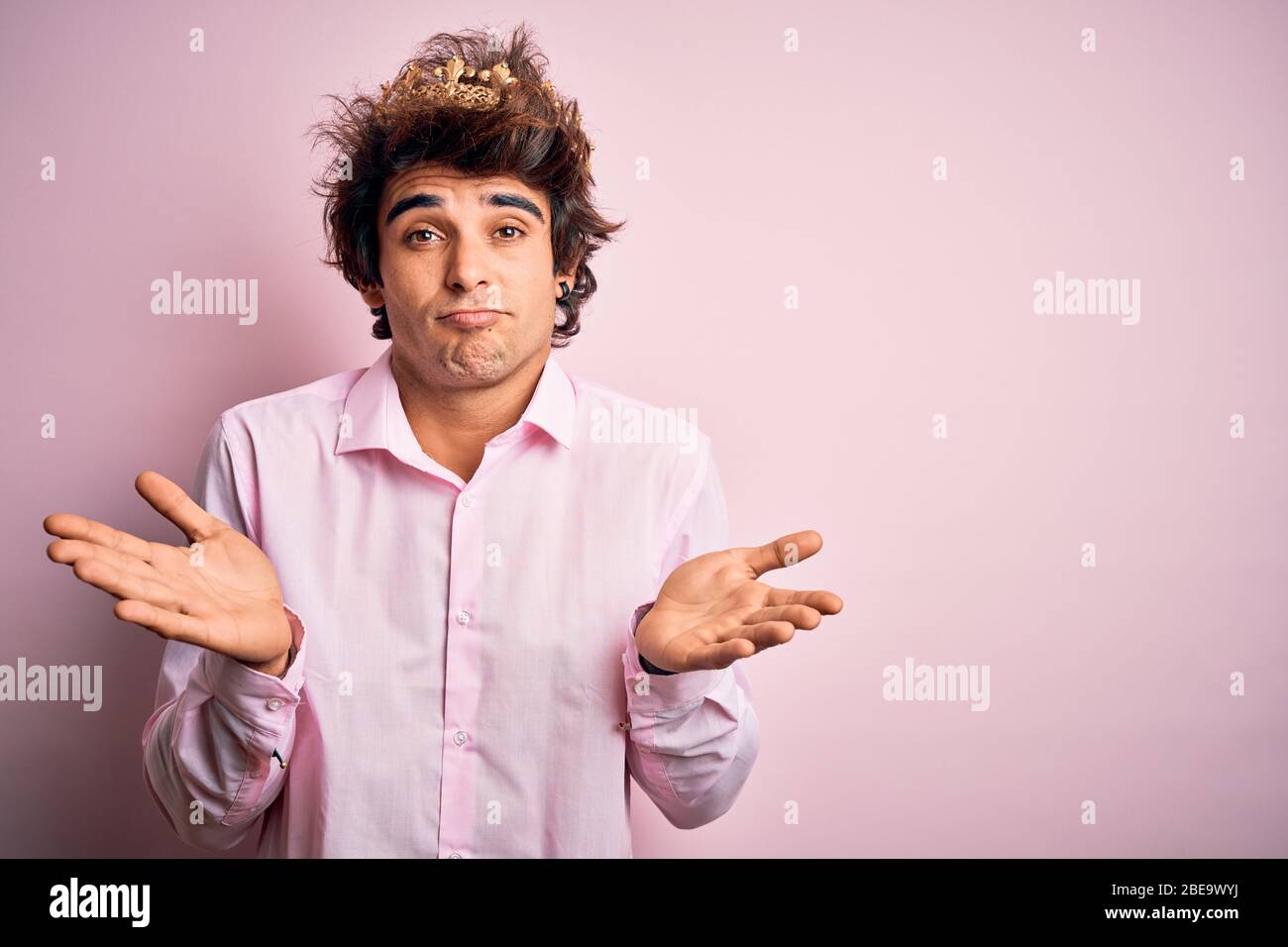 Young handsome man wearing king crown standing over isolated pink ...
