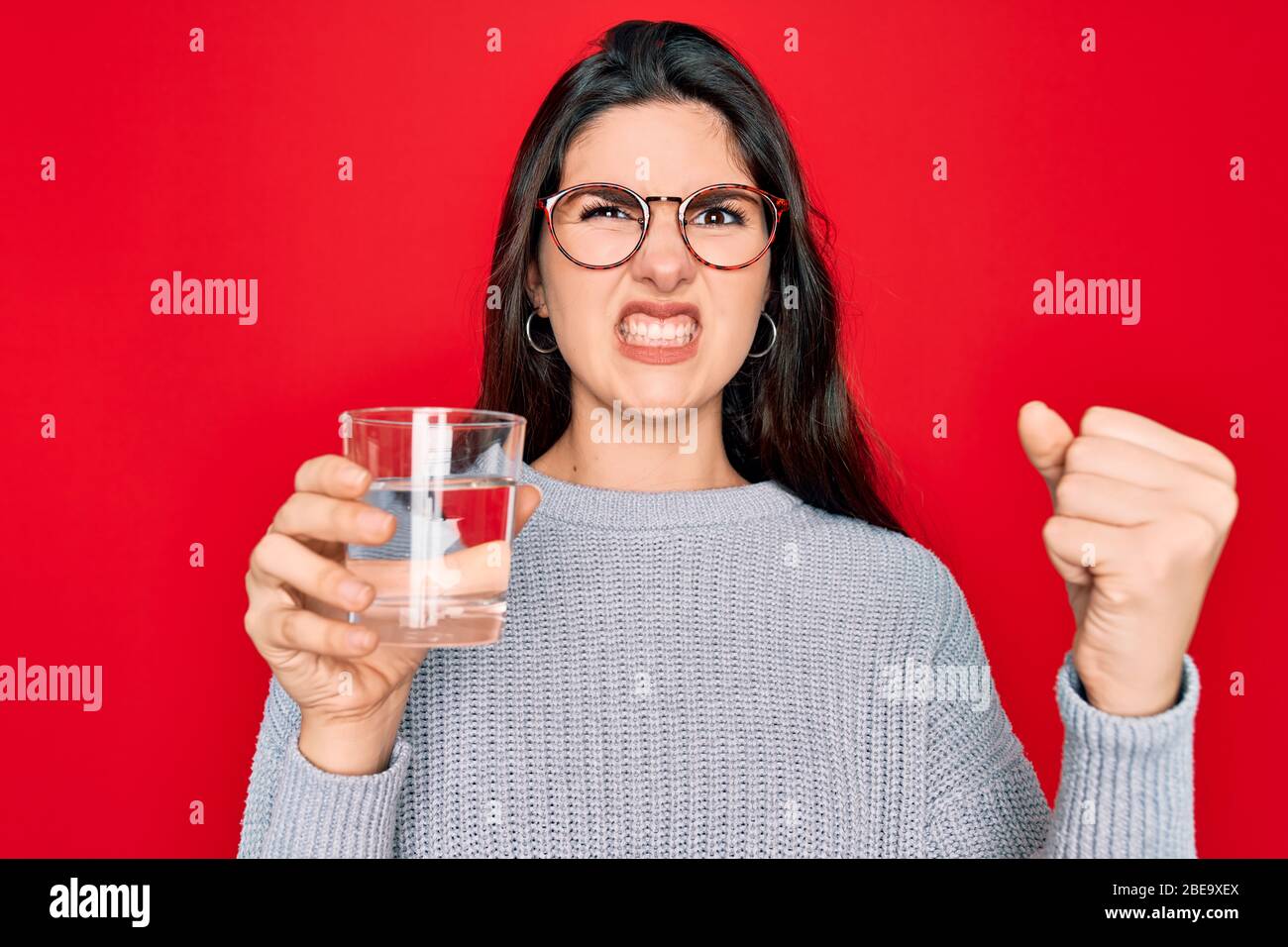 Young beautiful woman drinking a glass of fresh water over isolated red ...