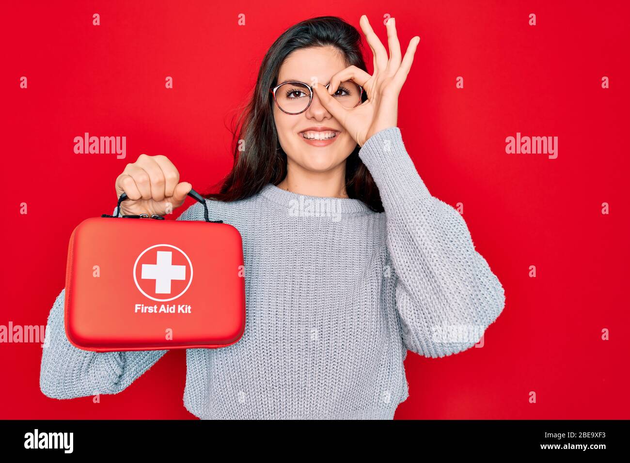 Young beautiful girl holding first aid kit medical box over red ...