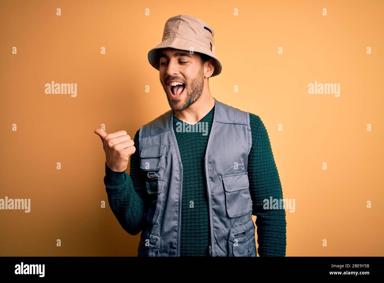 Handsome tourist man with beard on vacation wearing explorer hat over ...