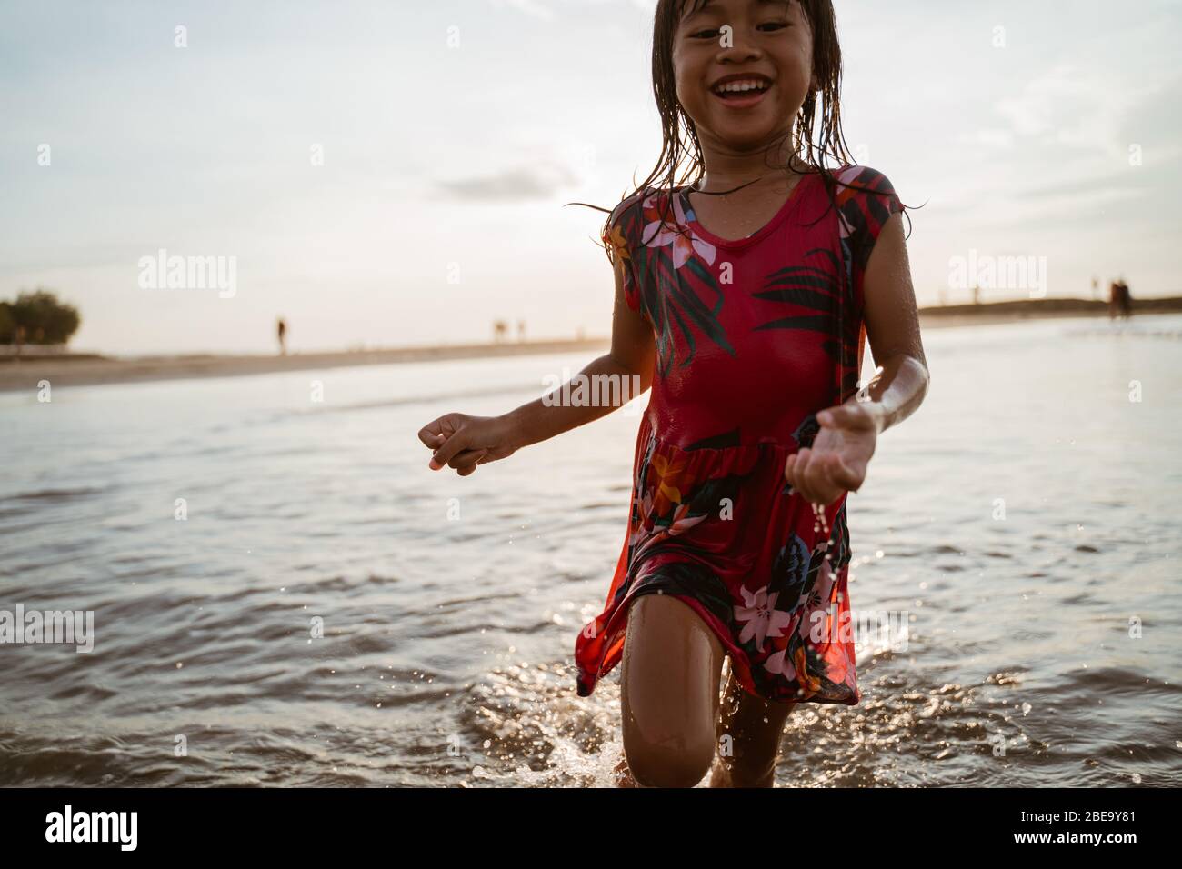 Little girl running on the beach while playing water on a beautiful ...