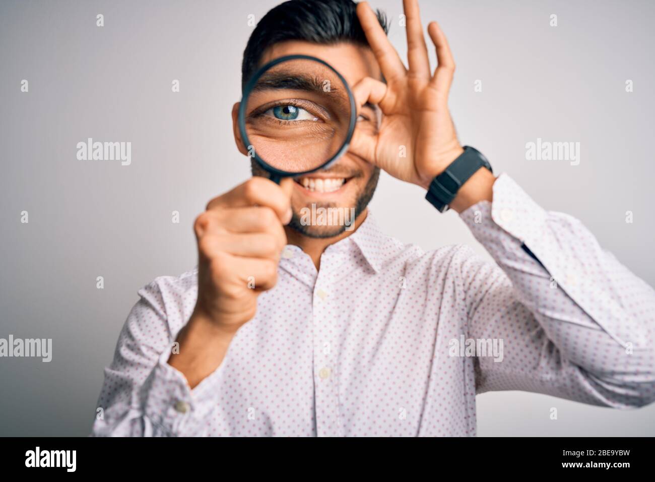 Young detective man looking through magnifying glass over isolated ...