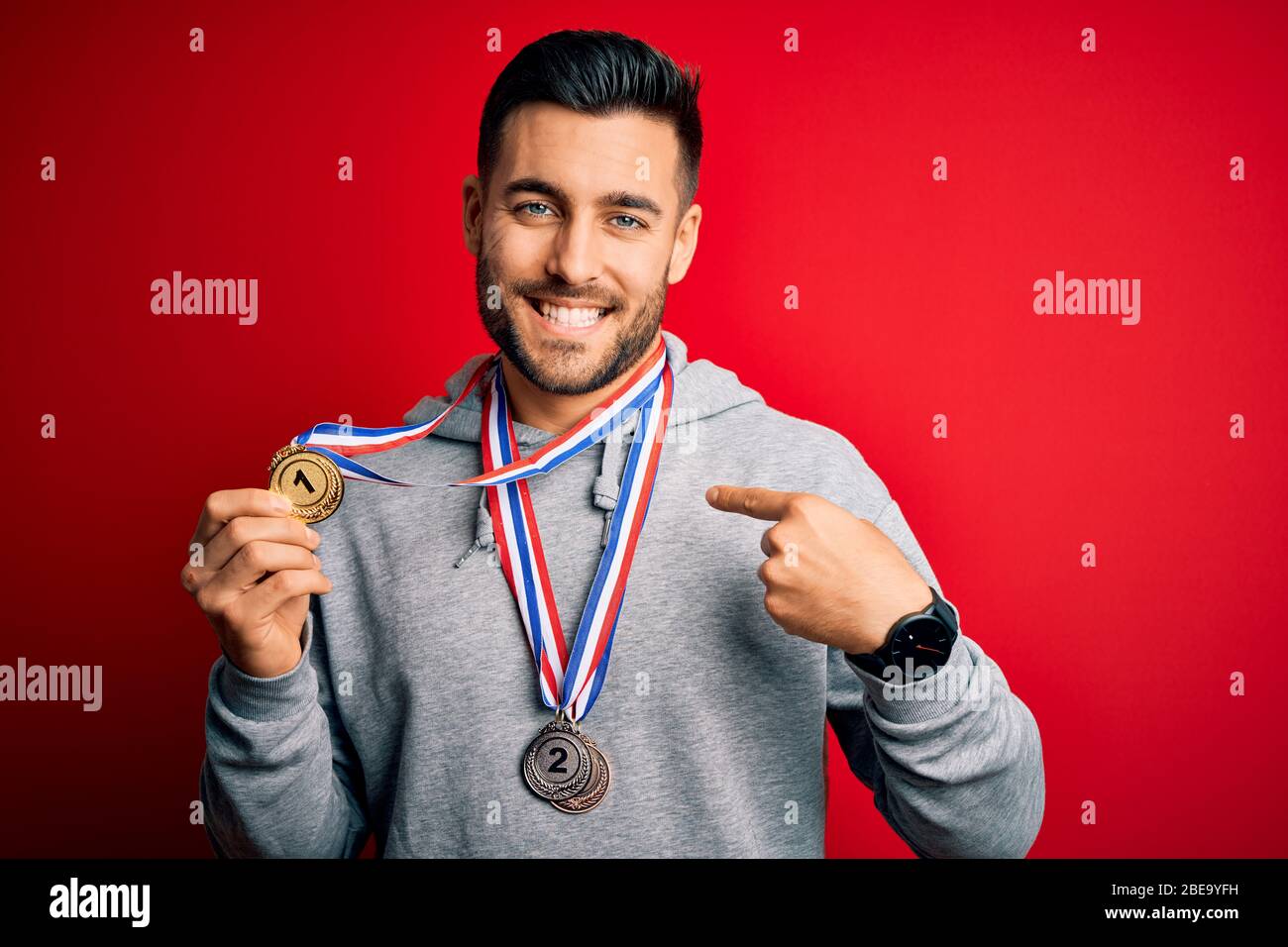Young handsome succesful man winning medals standing over isolated red ...