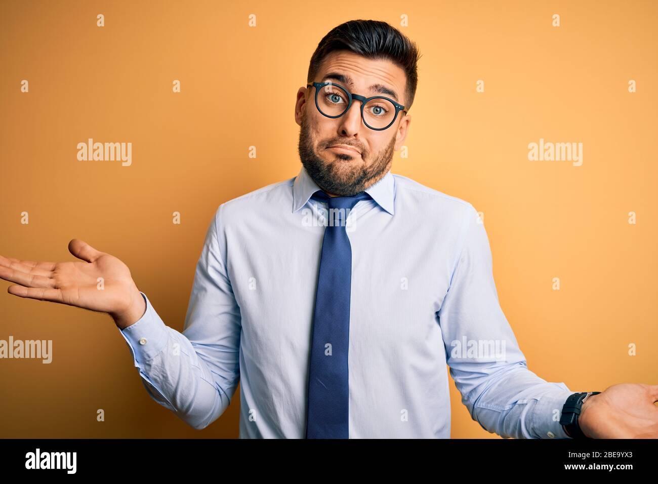 Young handsome businessman wearing tie and glasses standing over yellow ...