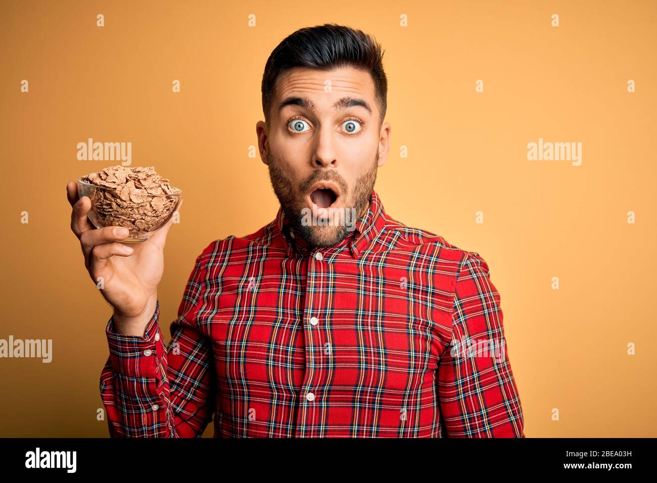 Young handsome man eating classic wholemeal cereals over yellow ...