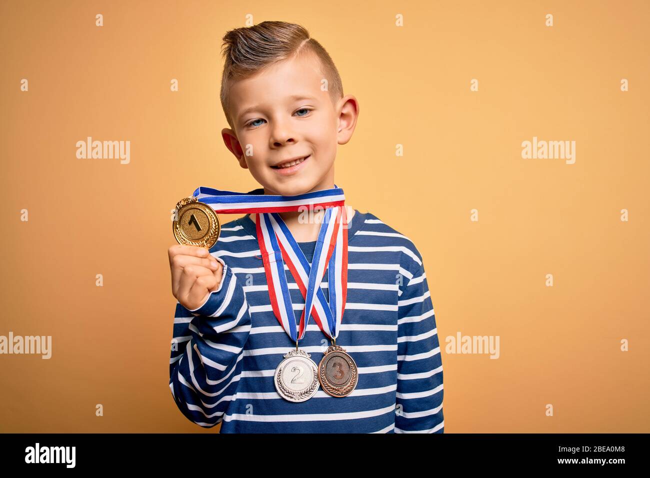 Young little caucasian winner kid wearing award competition medals over ...