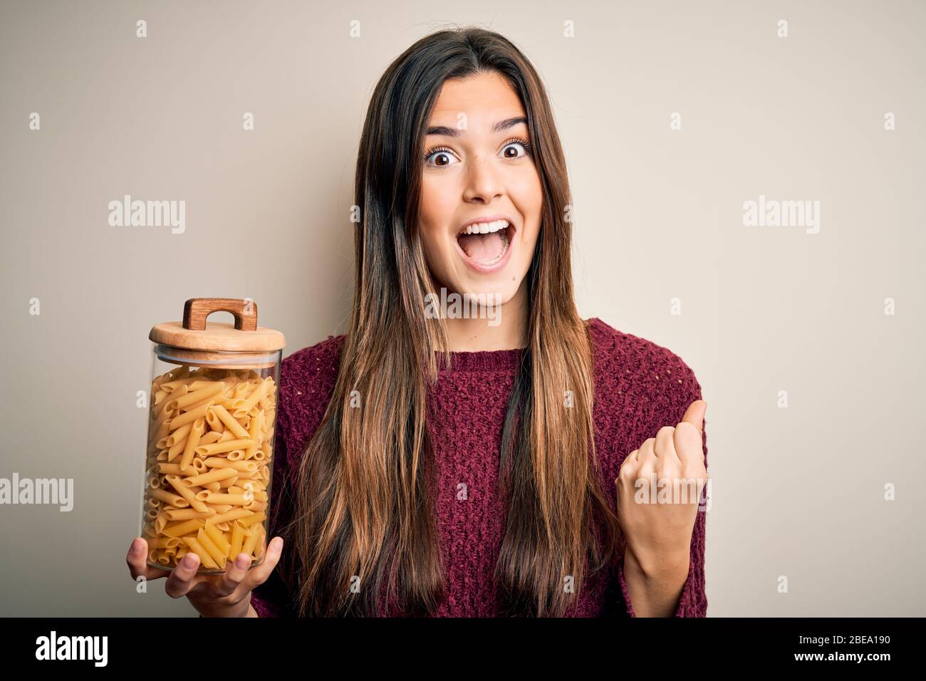 Young beautiful girl holding bottle of dry Italian pasta macaroni over ...