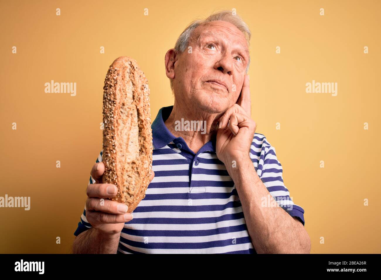 Grey haired senior man holding healthy wholemeal bread over yellow ...