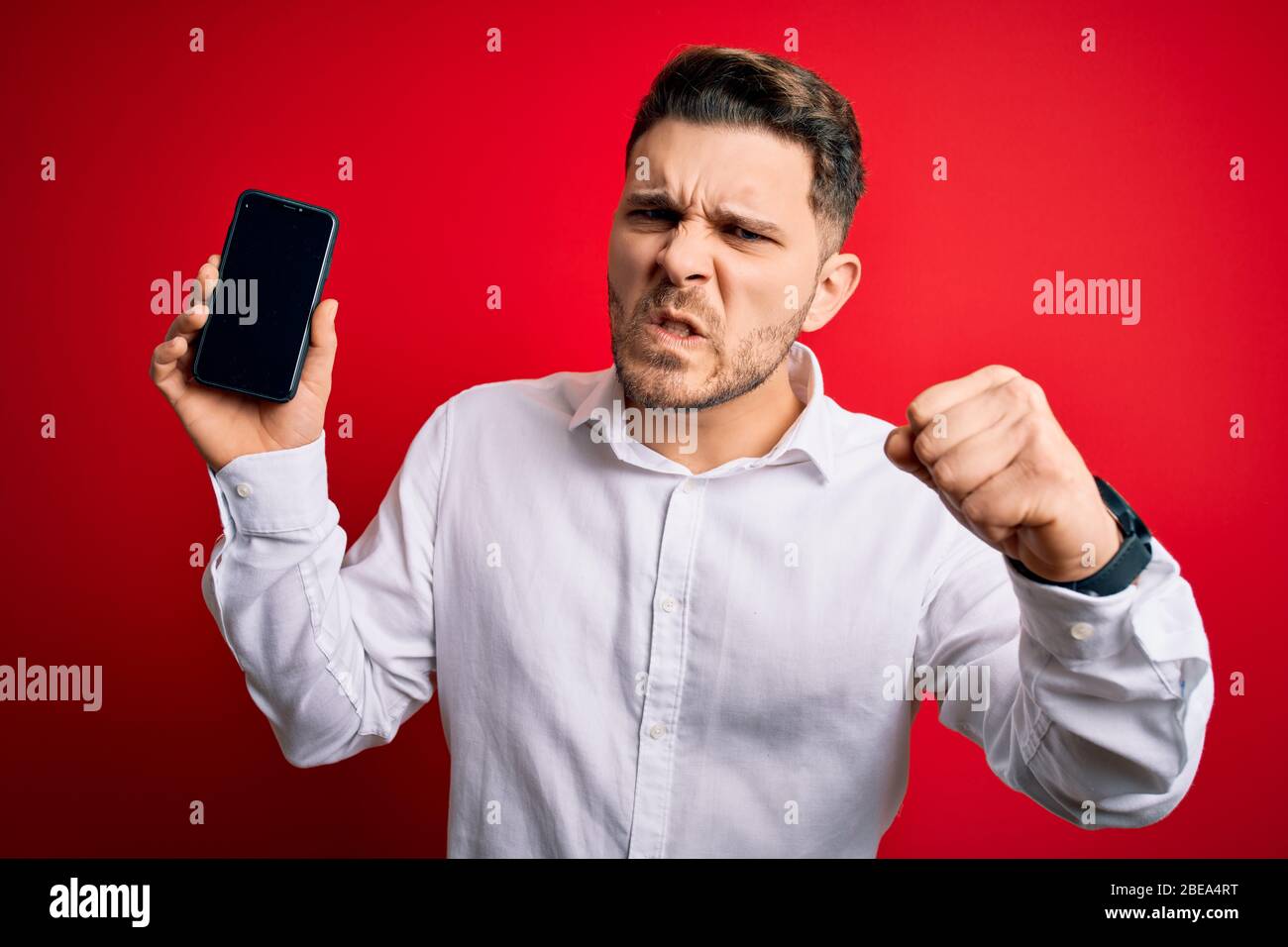 Young business man with blue eyes showing smartphone screen over red ...