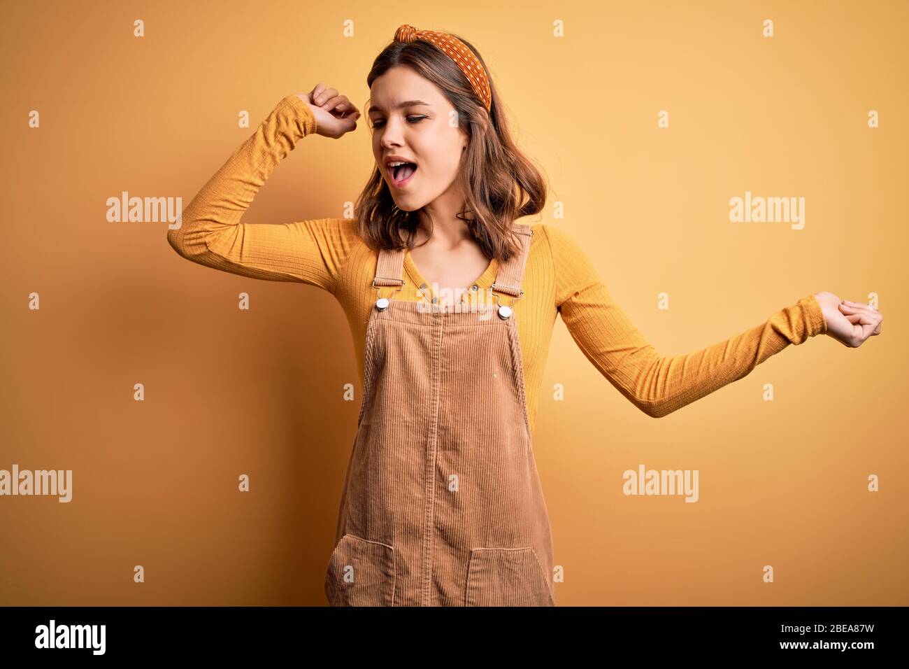 Young beautiful blonde girl wearing overall standing over yellow ...