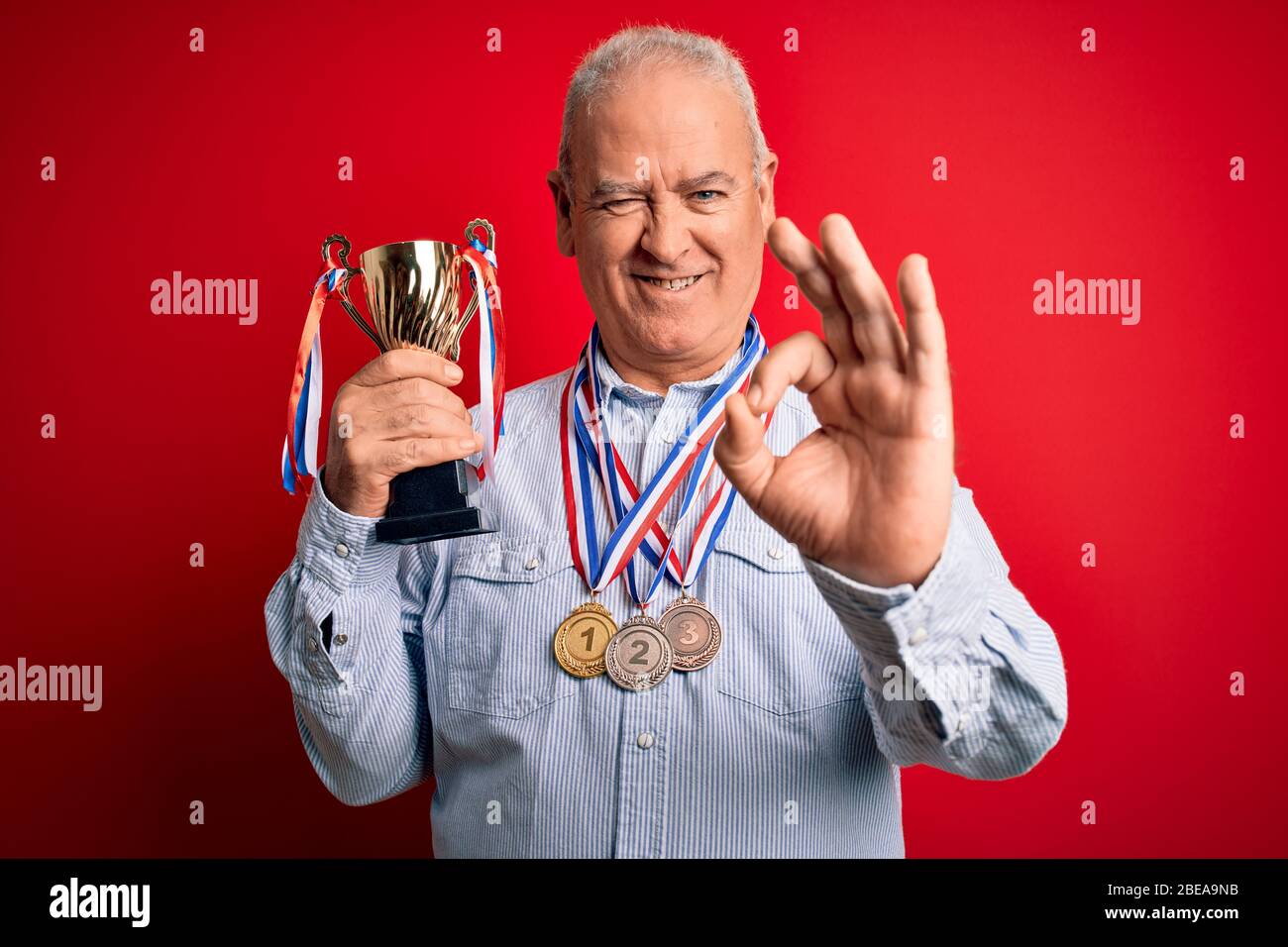Middle age hoary successful man wearing medals holding trophy over ...