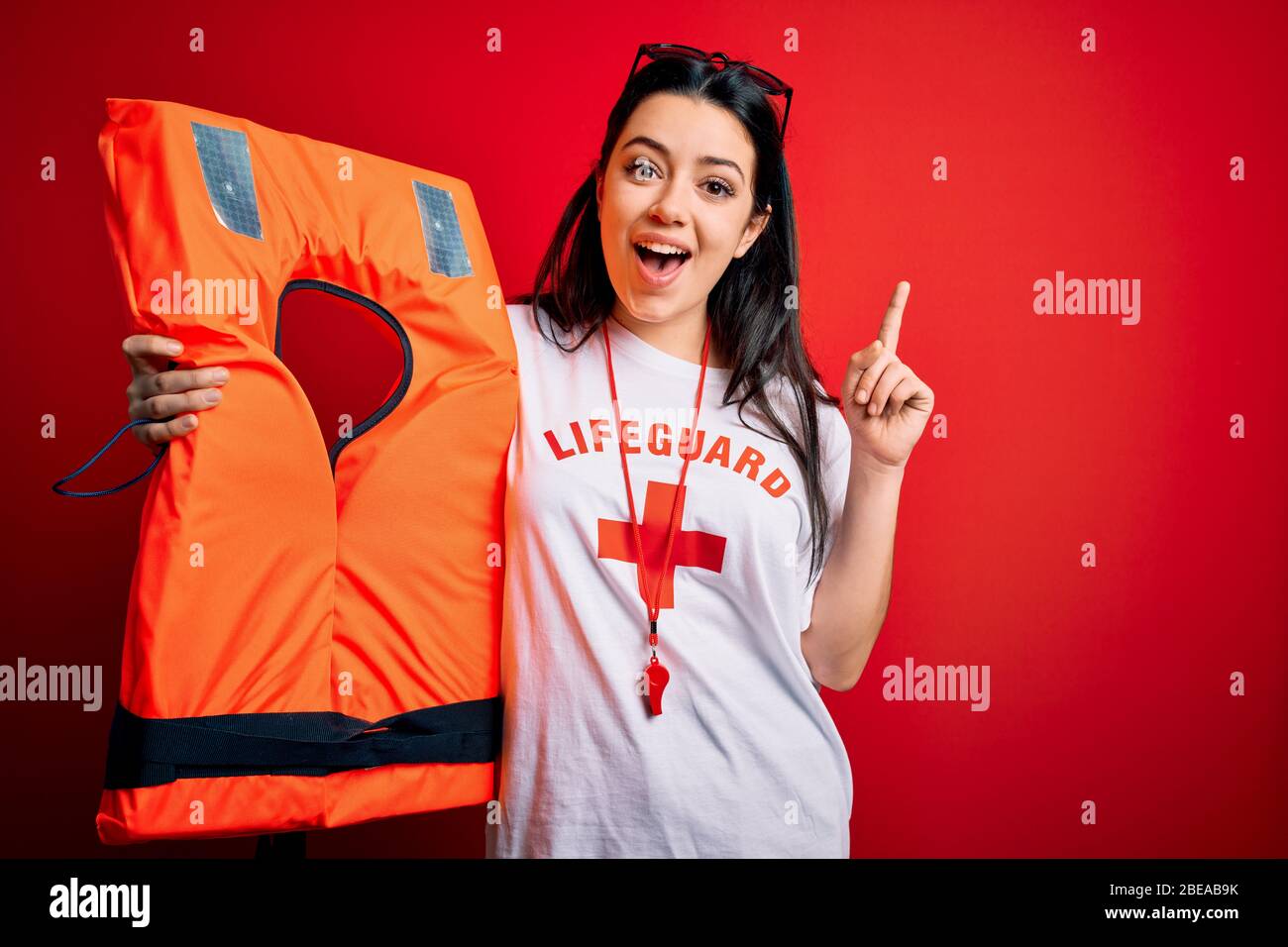 Young lifeguard woman holding rescue lifejacket over red background ...