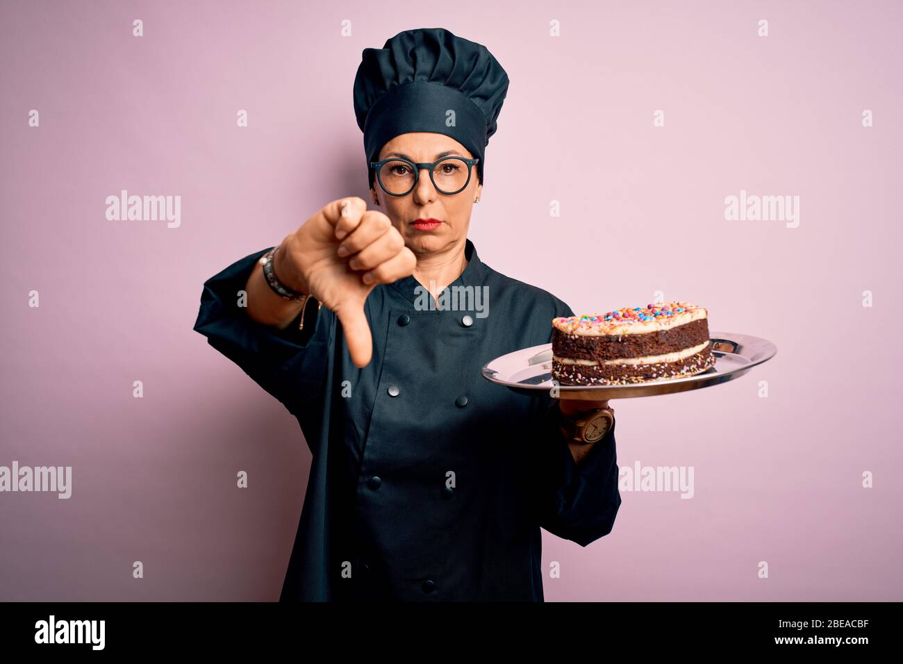 Middle age baker woman wearing cooker uniform and hat holding tray with ...