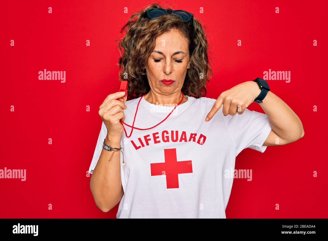 Middle age senior summer lifeguard woman holding whistle over red ...