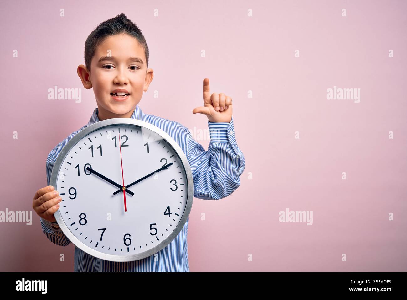 Young little boy kid holding big minute clock over isolated pink ...