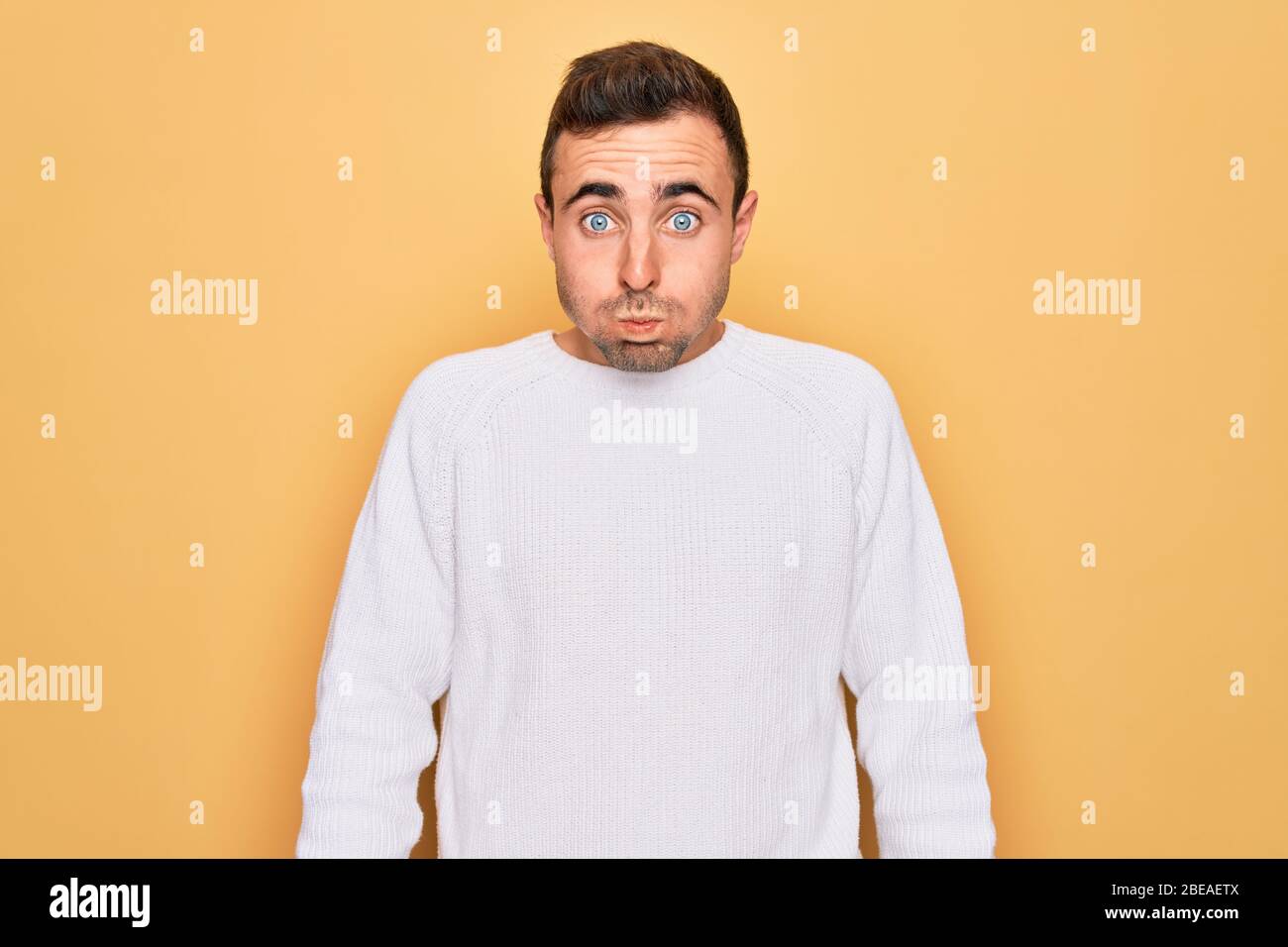 Young handsome man with blue eyes wearing casual sweater standing over ...
