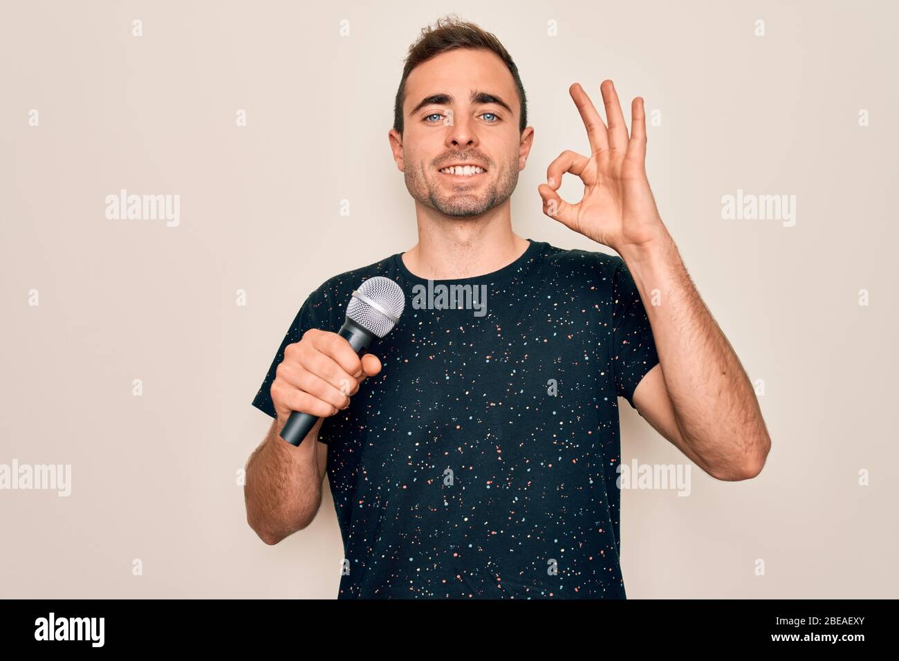 Young handsome singer man with blue eyes singing using microphone over white background doing ok ...