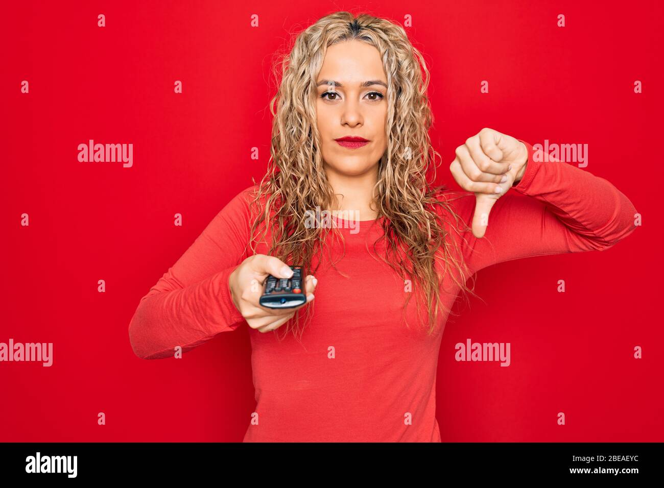 Young beautiful blonde woman using television remote control over ...