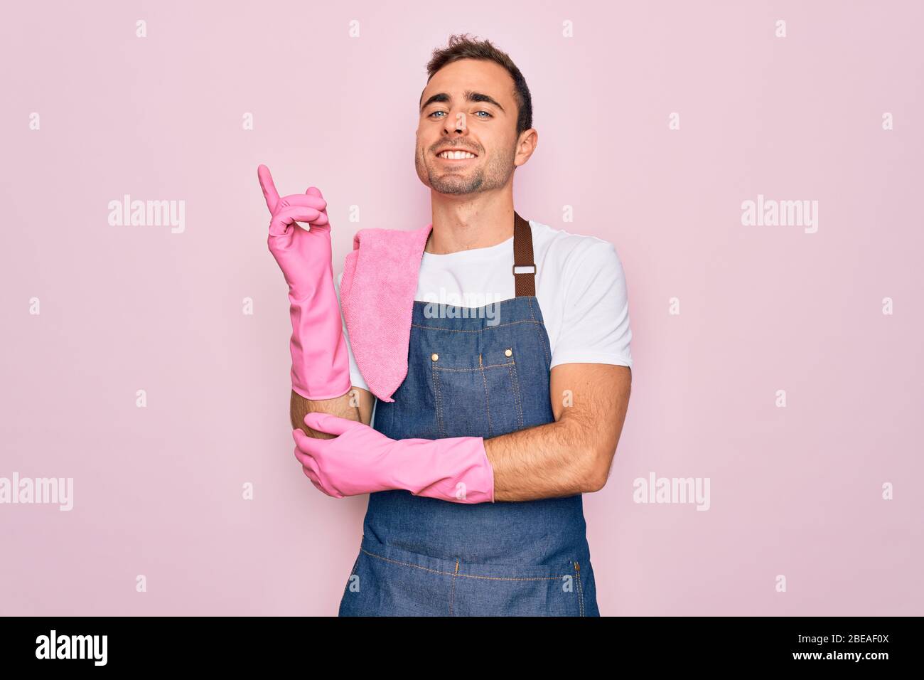 Young cleaner man with blue eyes cleaning wearing apron and gloves over ...