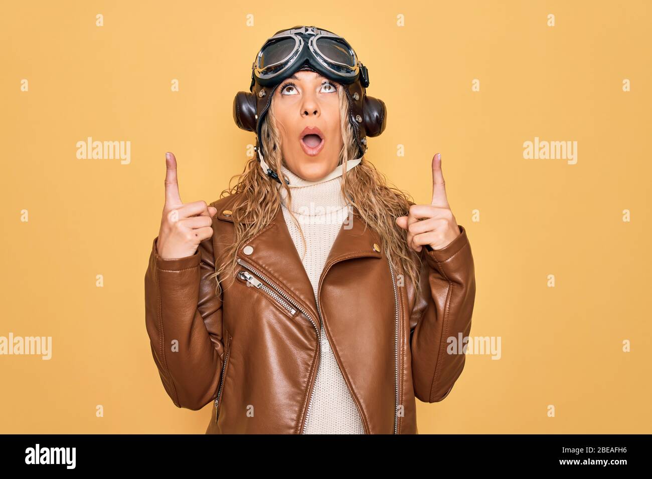 Young beautiful blonde aviator woman wearing vintage pilot helmet whit ...