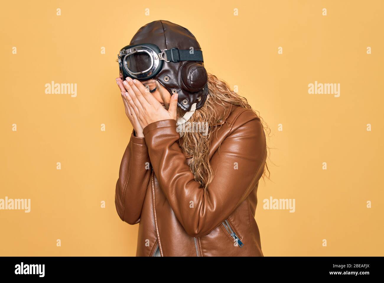 Young beautiful blonde aviator woman wearing vintage pilot helmet whit ...