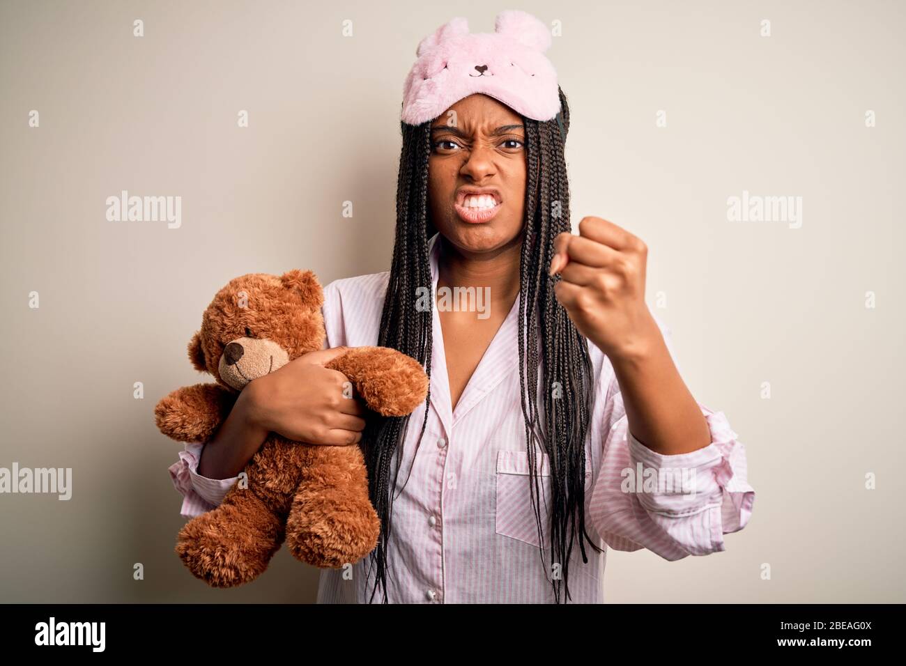 Young african american woman wearing pajama and eye mask hugging teddy ...