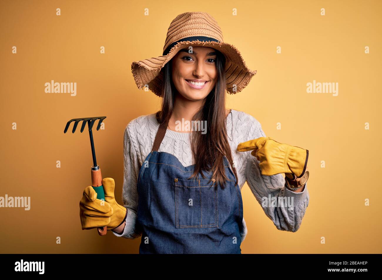 Young beautiful farmer woman wearing apron and hat using rake over ...