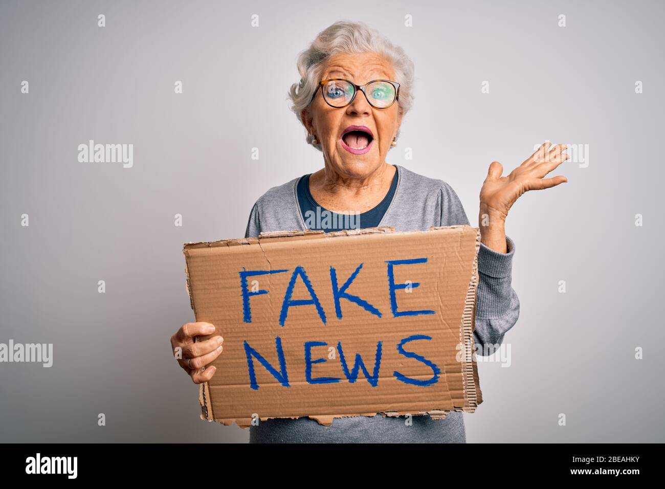 Senior grey-haired woman holding banner with fake news message over ...