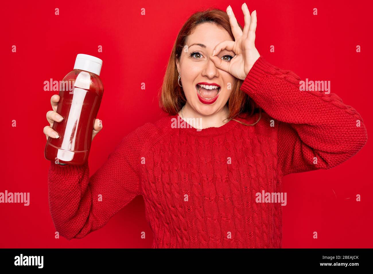 Beautiful redhead woman holding bottle of ketchup sauce condiment over ...