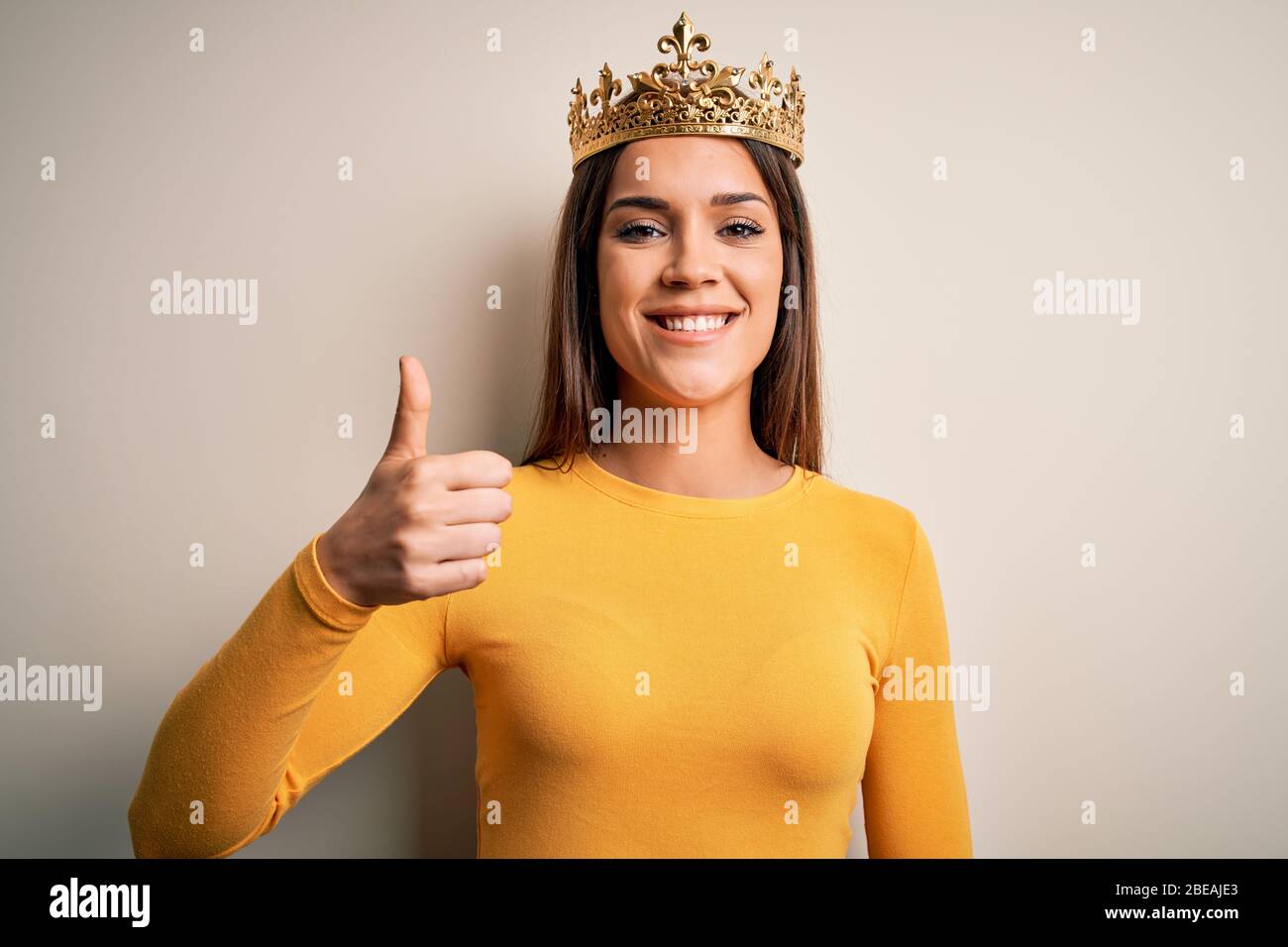 Young beautiful brunette woman wearing golden queen crown over white ...