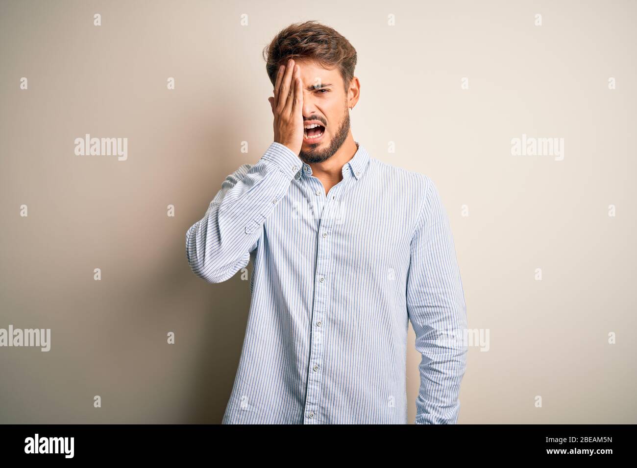 Young handsome man with beard wearing striped shirt standing over white ...