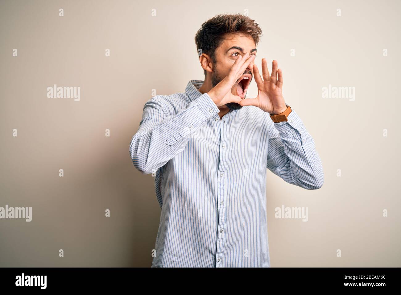 Young handsome man with beard wearing striped shirt standing over white ...
