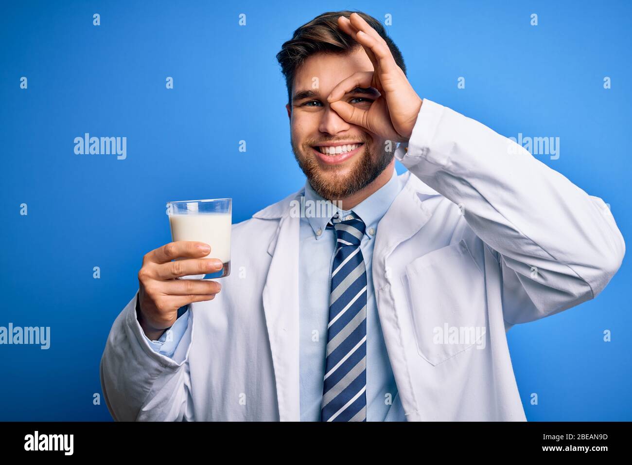 Young blond doctor man with beard and blue eyes wearing coat drinking ...