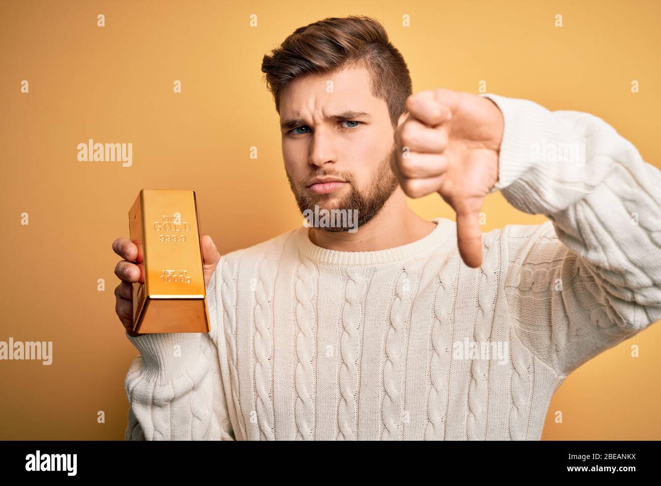 Young blond man with beard and blue eyes holding gold ingot over ...